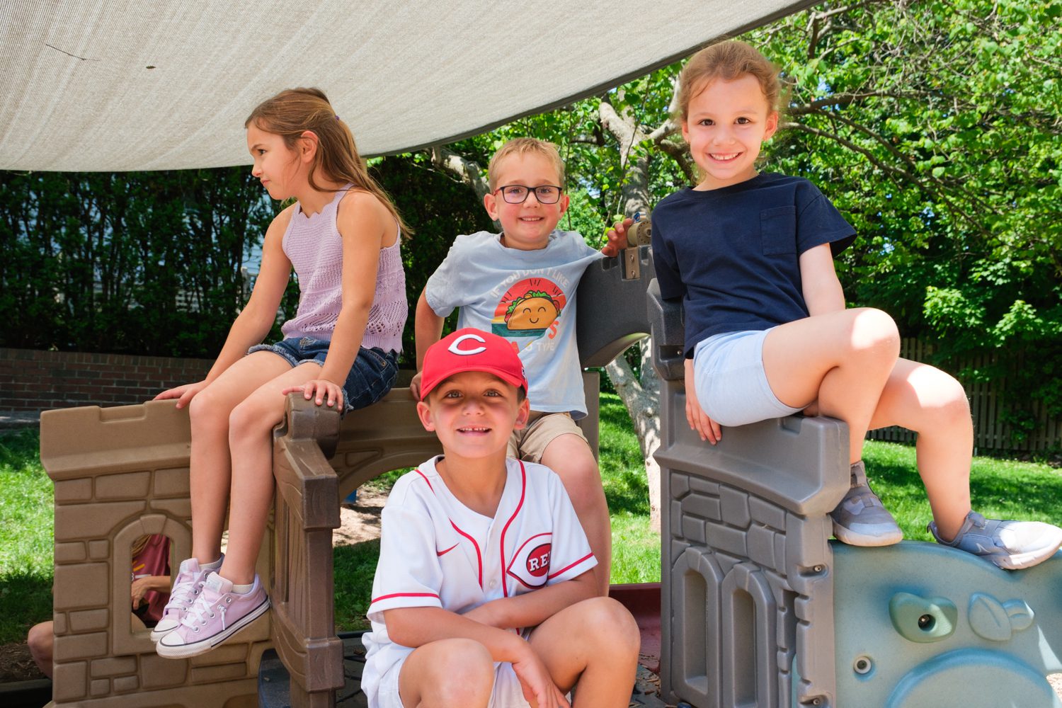 Four children playing outdoors on playground equipment under a shaded ...